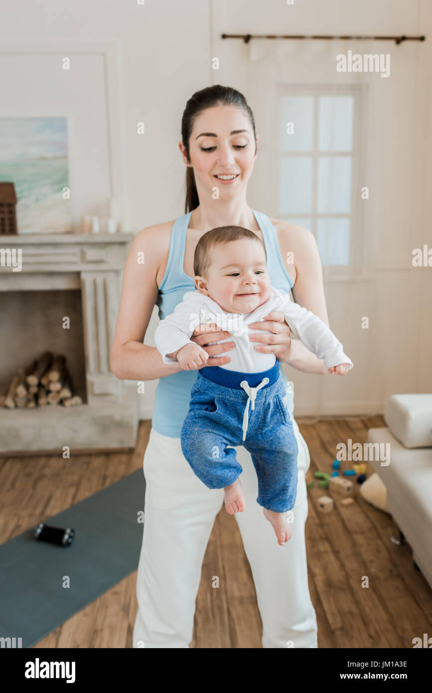 Portrait of smiling woman carrying her happy baby child on arms and ...
