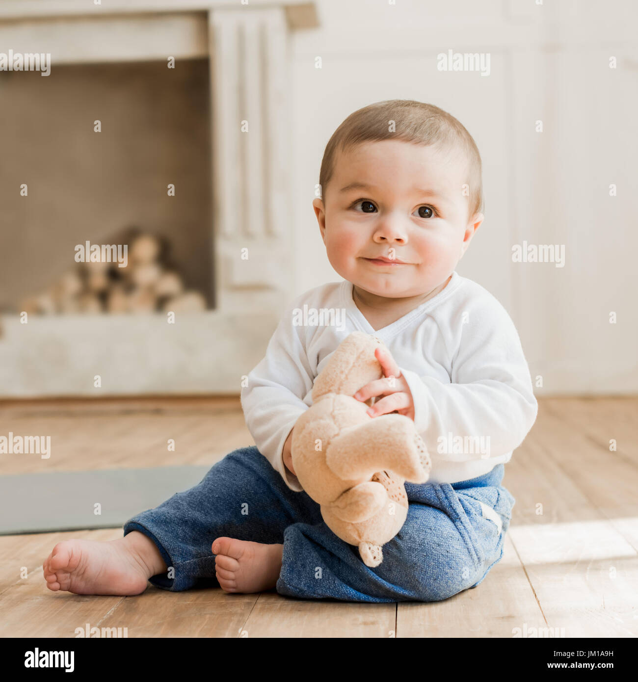 Smiling baby boy sitting with teddy bear toy on the floor Stock Photo ...