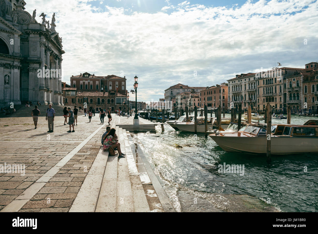 Tourists sit on the steps of Grand Canal. Venice is a popular tourist ...