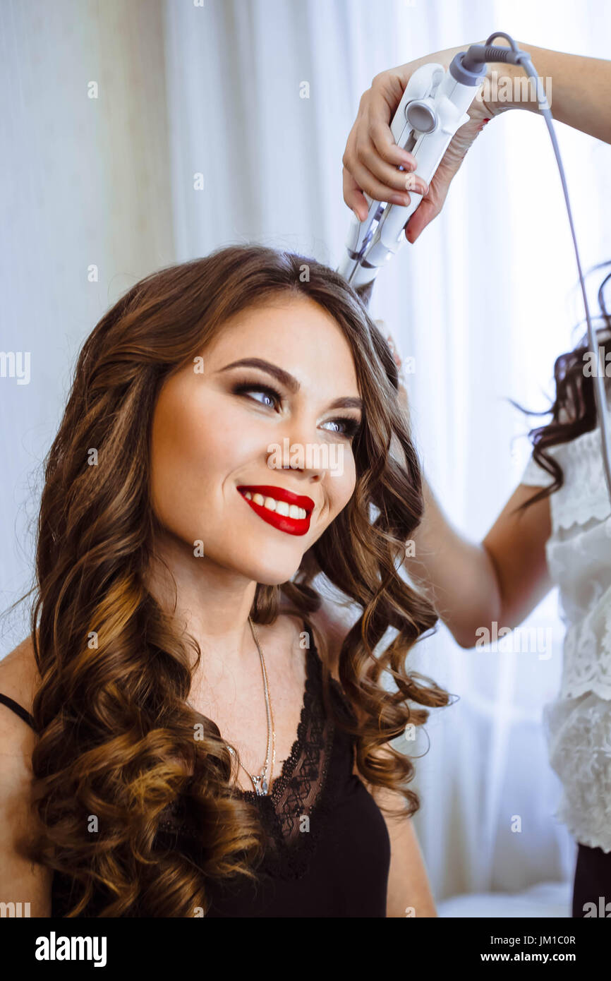 Hair stylist making ringlets to brunette woman. Hairdresser working ...