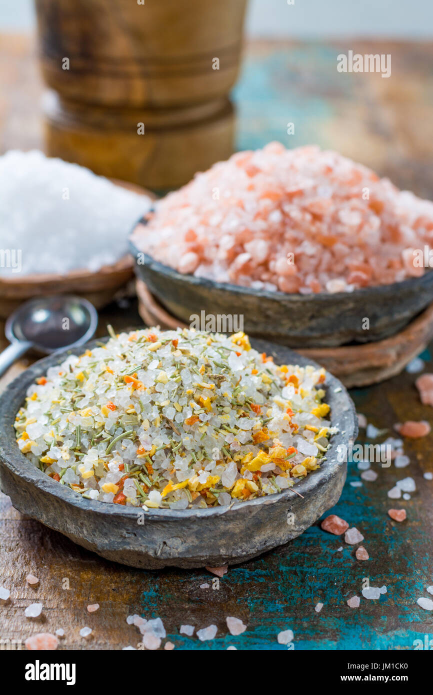 Different types of natural salt in stone bowls on wooden surface. White ...