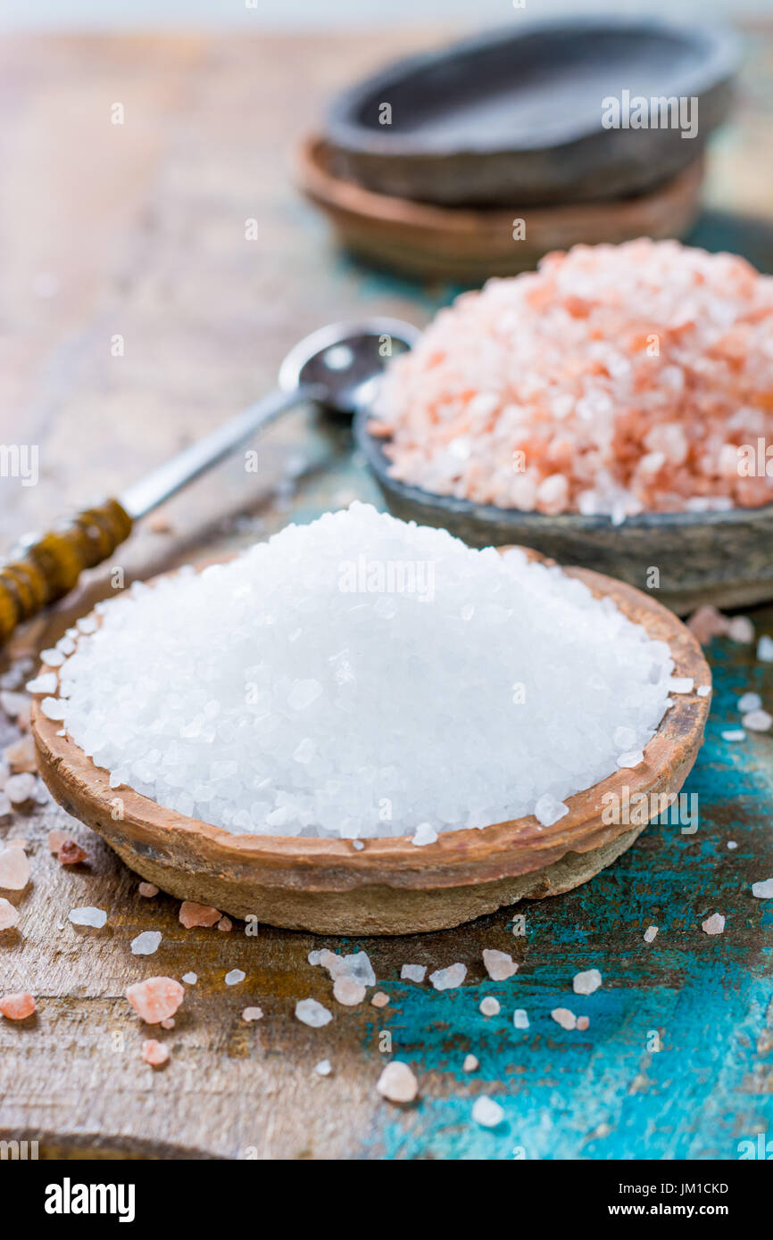 Different types of natural salt in stone bowls on wooden surface. White ...