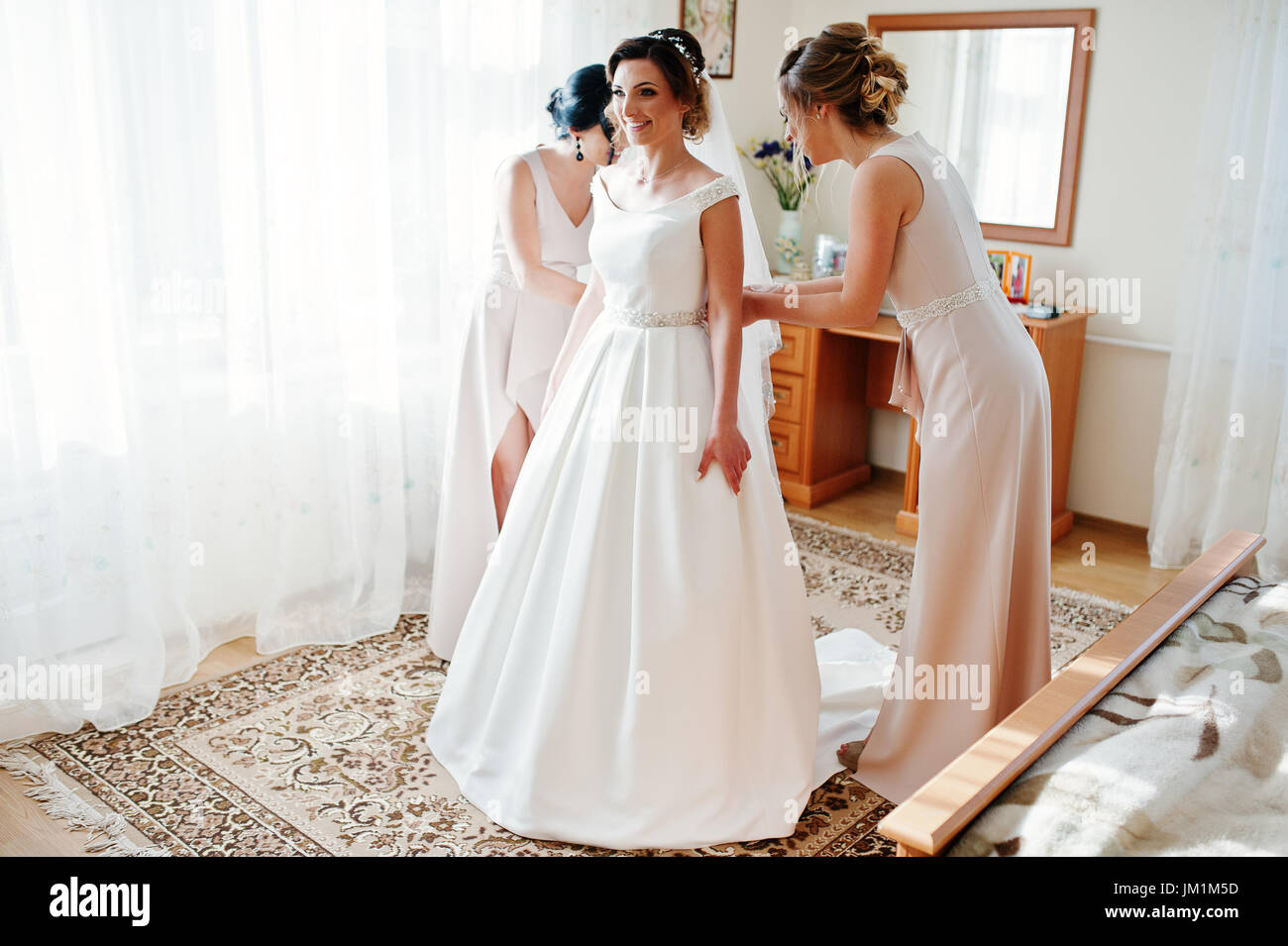 Bridesmaids helping gorgeous bride to dress up and get ready for her ...