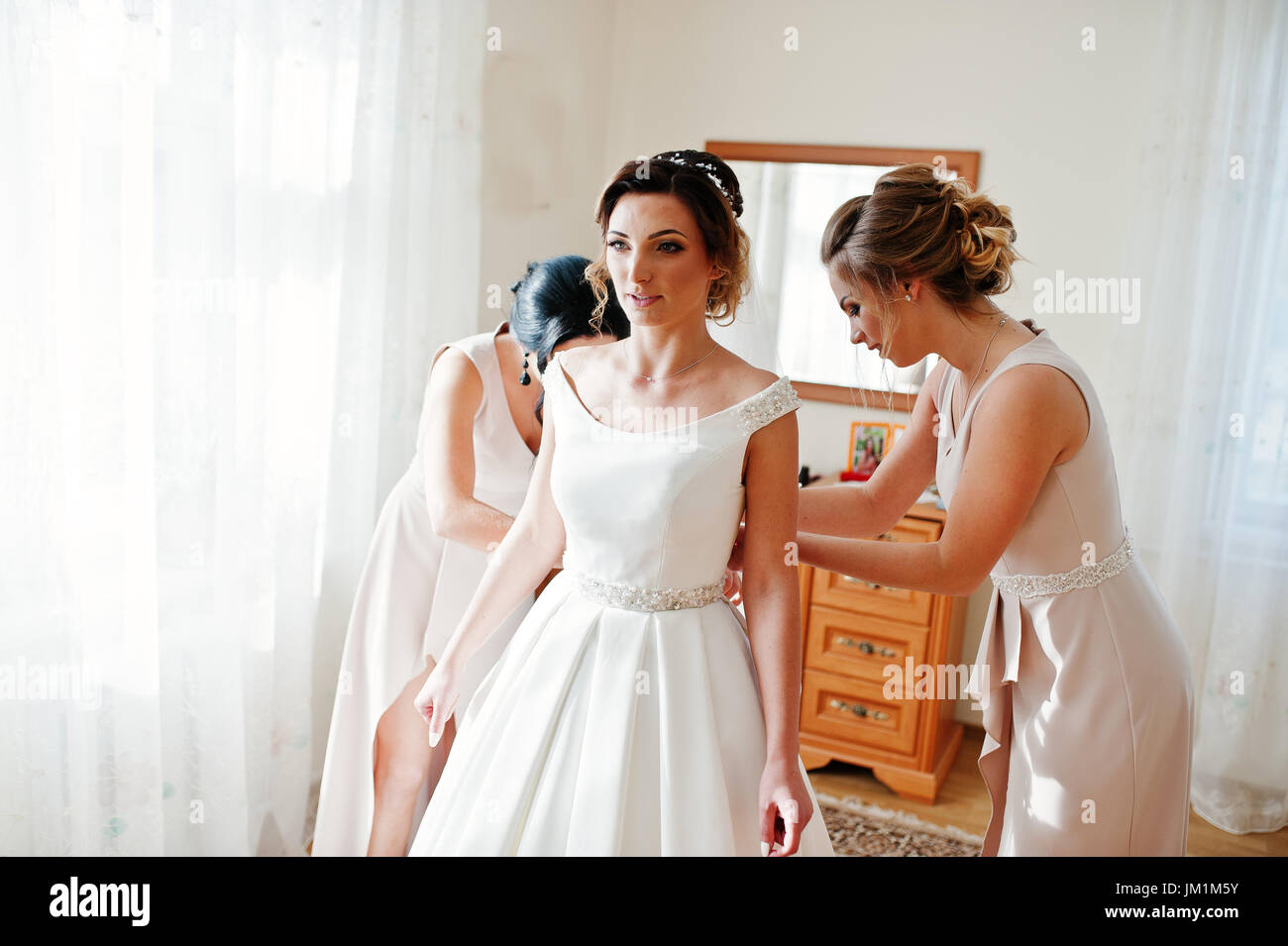 Bridesmaids helping gorgeous bride to dress up and get ready for her ...