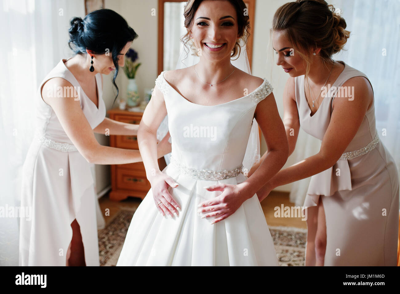 Bridesmaids helping gorgeous bride to dress up and get ready for her ...