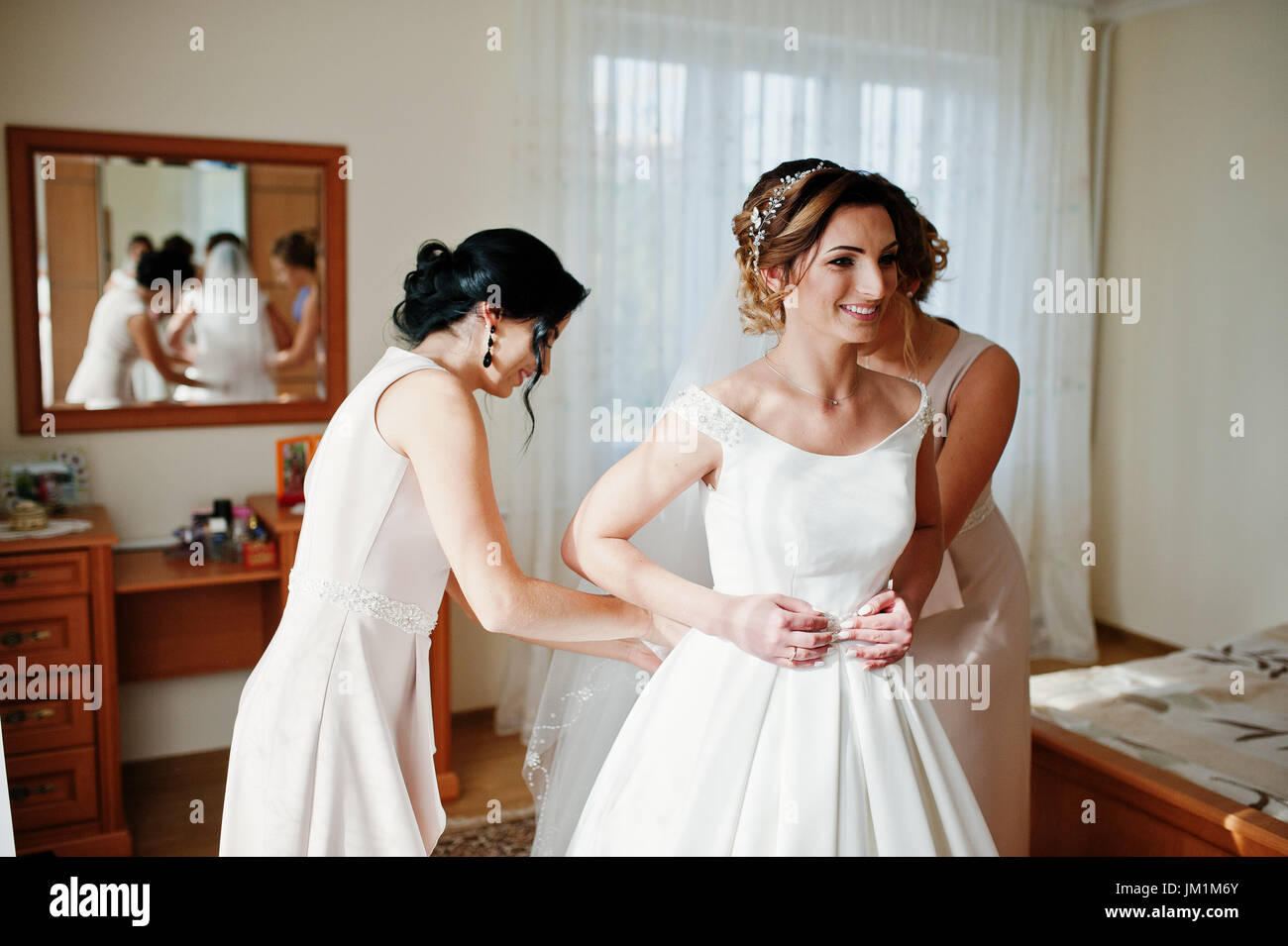 Bridesmaids helping gorgeous bride to dress up and get ready for her ...