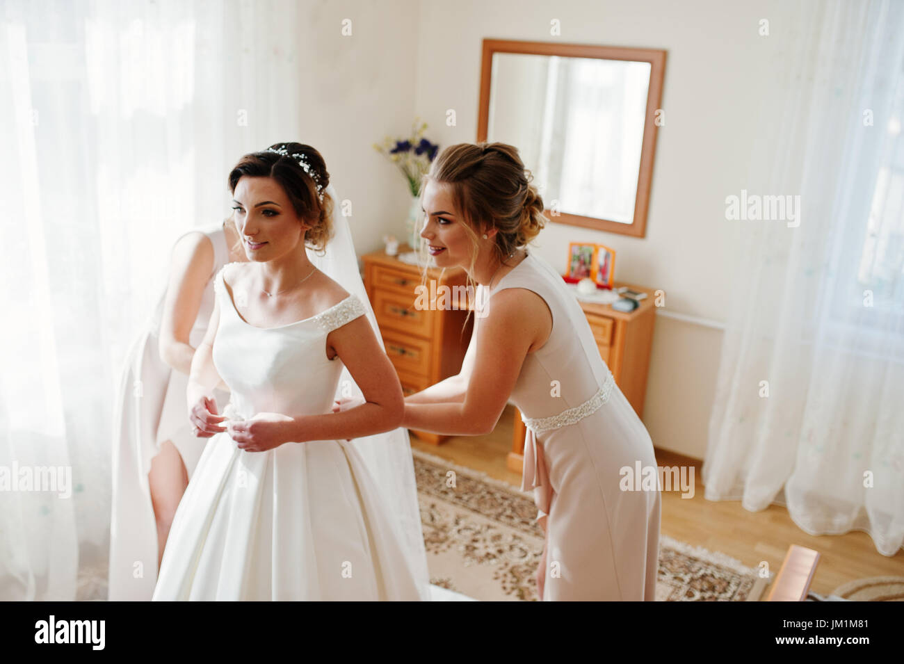 Bridesmaids helping gorgeous bride to dress up and get ready for her ...