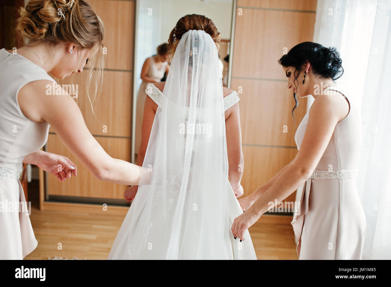 Bridesmaids helping gorgeous bride to dress up and get ready for her ...