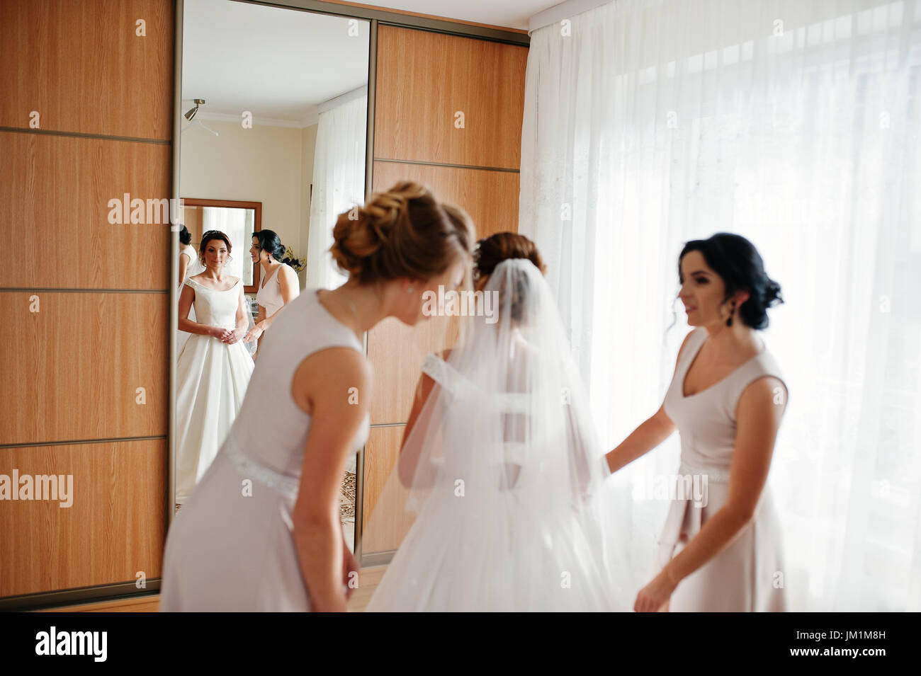 Bridesmaids helping gorgeous bride to dress up and get ready for her ...