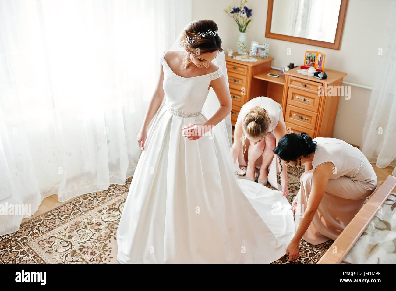 Bridesmaids helping gorgeous bride to dress up and get ready for her ...