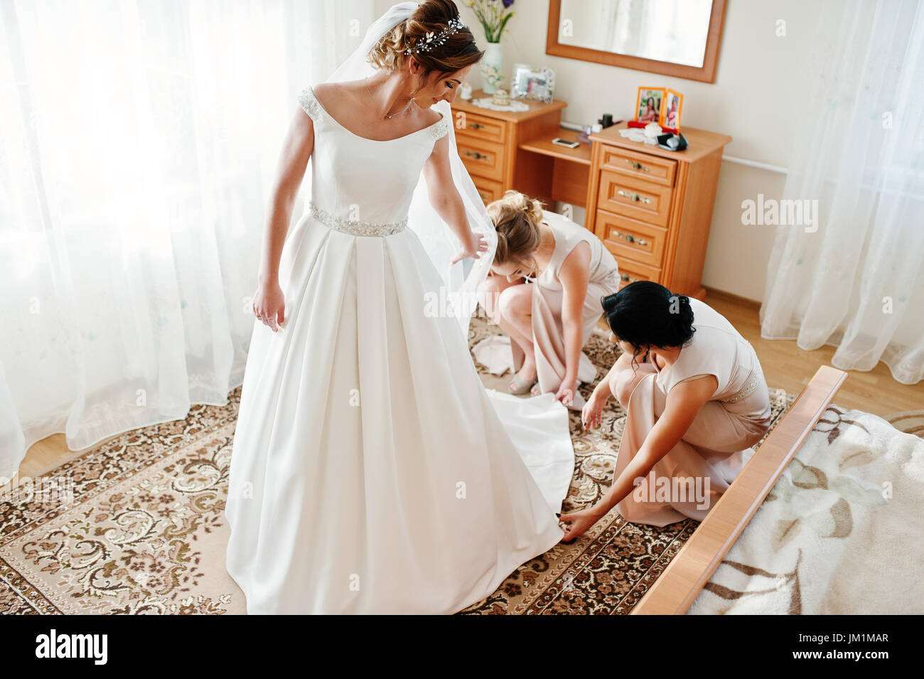 Bridesmaids helping gorgeous bride to dress up and get ready for her ...