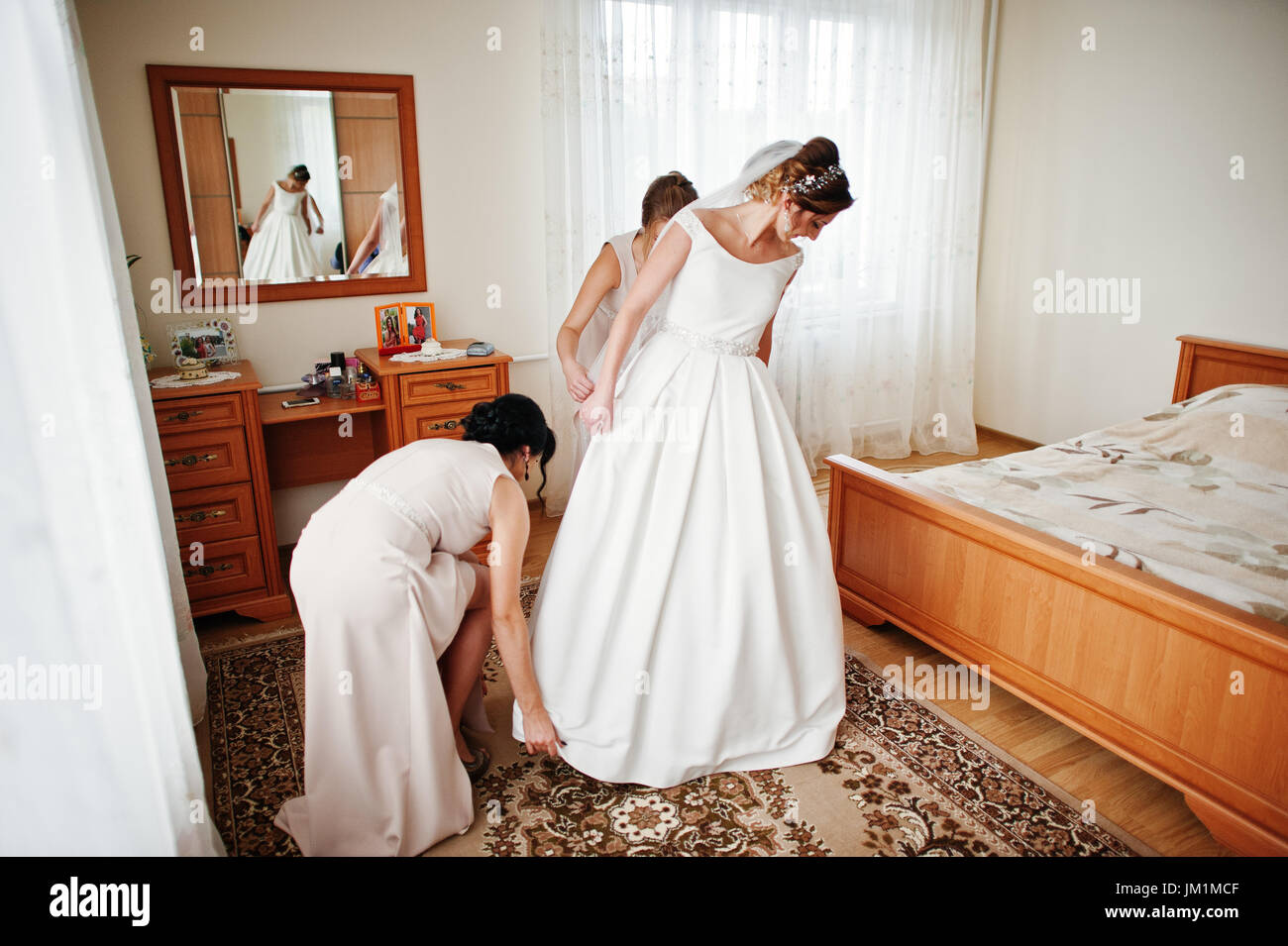 Bridesmaids helping gorgeous bride to dress up and get ready for her ...