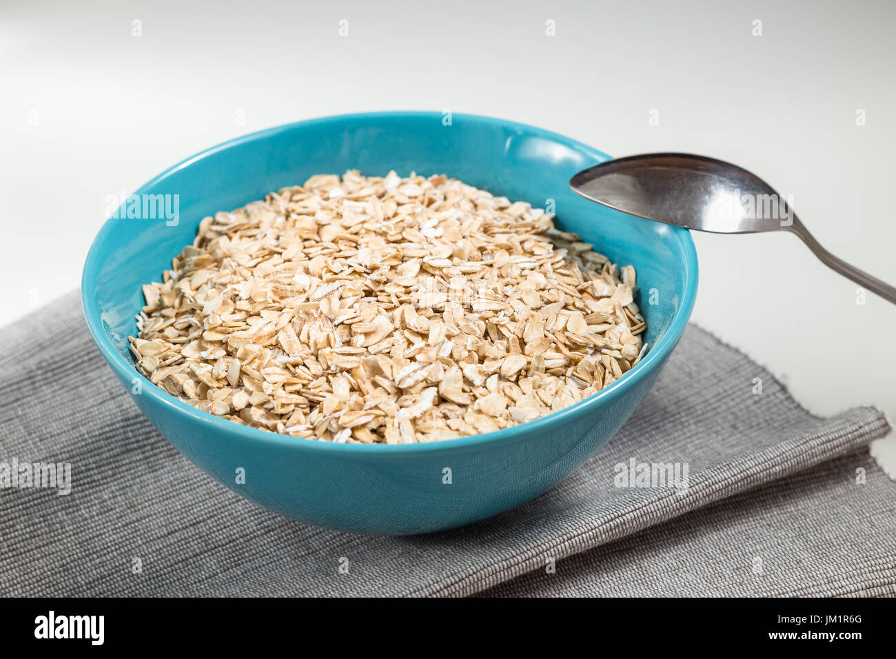 Oat flakes in blue ceramic bowl ready to cook and spoon on the white ...