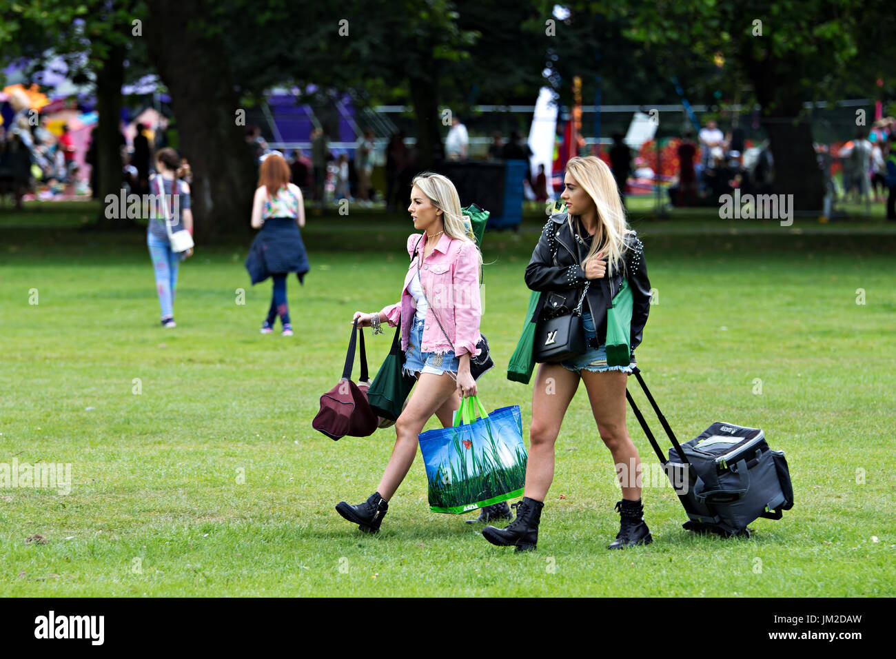 Two girls arriving at an outdoor music festival carrying their supplies ...