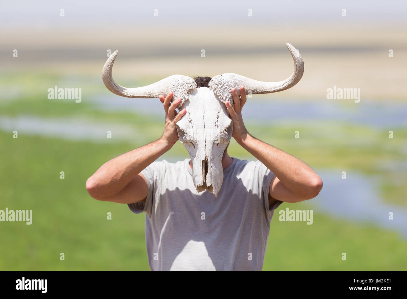 Man holding a white wildebeest skull wearing it like a mask in nature ...