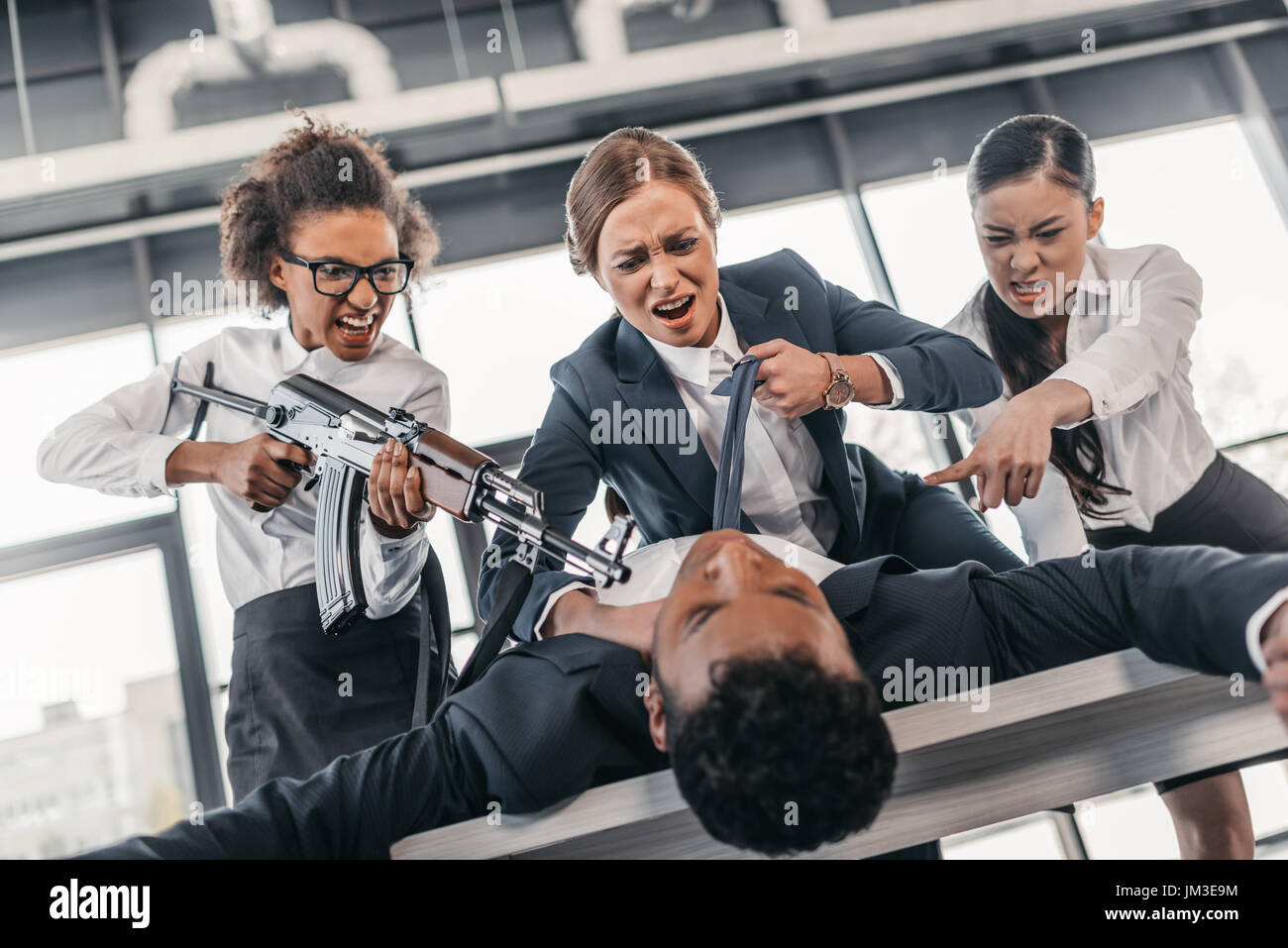 Three young angry businesswomen with rifle punishing businessman lying ...