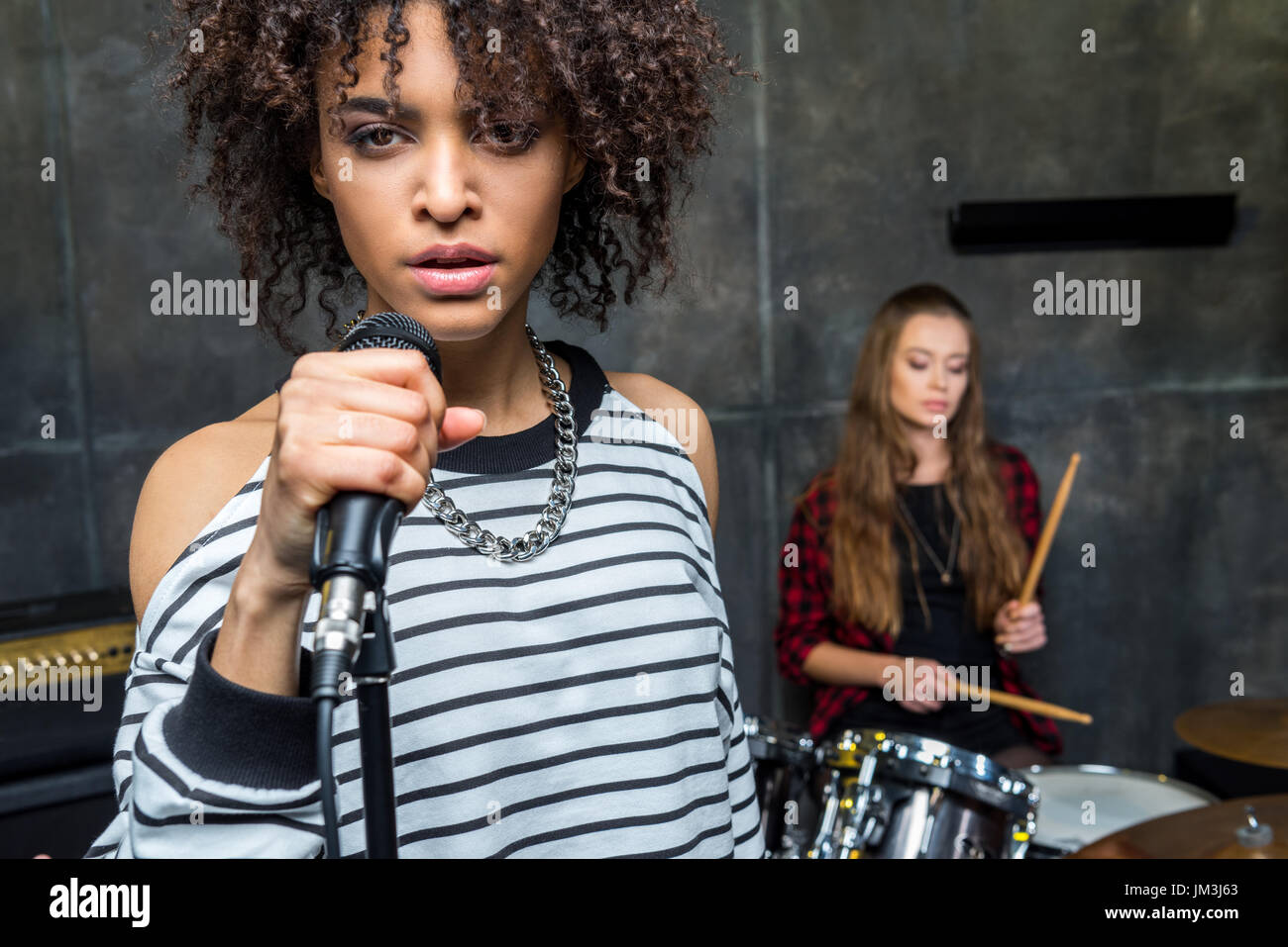 Young singer standing with microphone while friend playing drums, hard ...