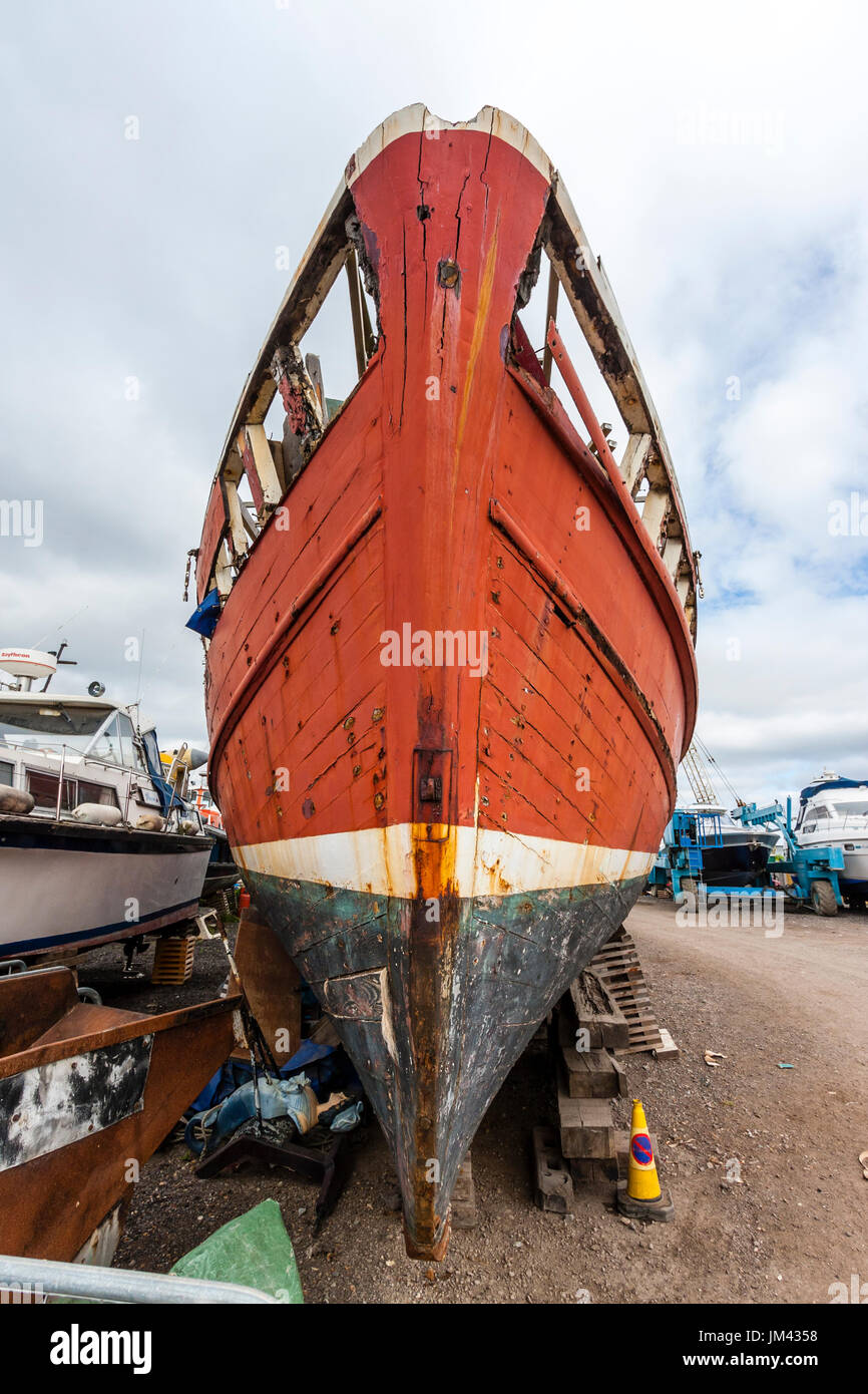 Matt red painted bows of old dry-docked boat. Woodwork crumbling with ...