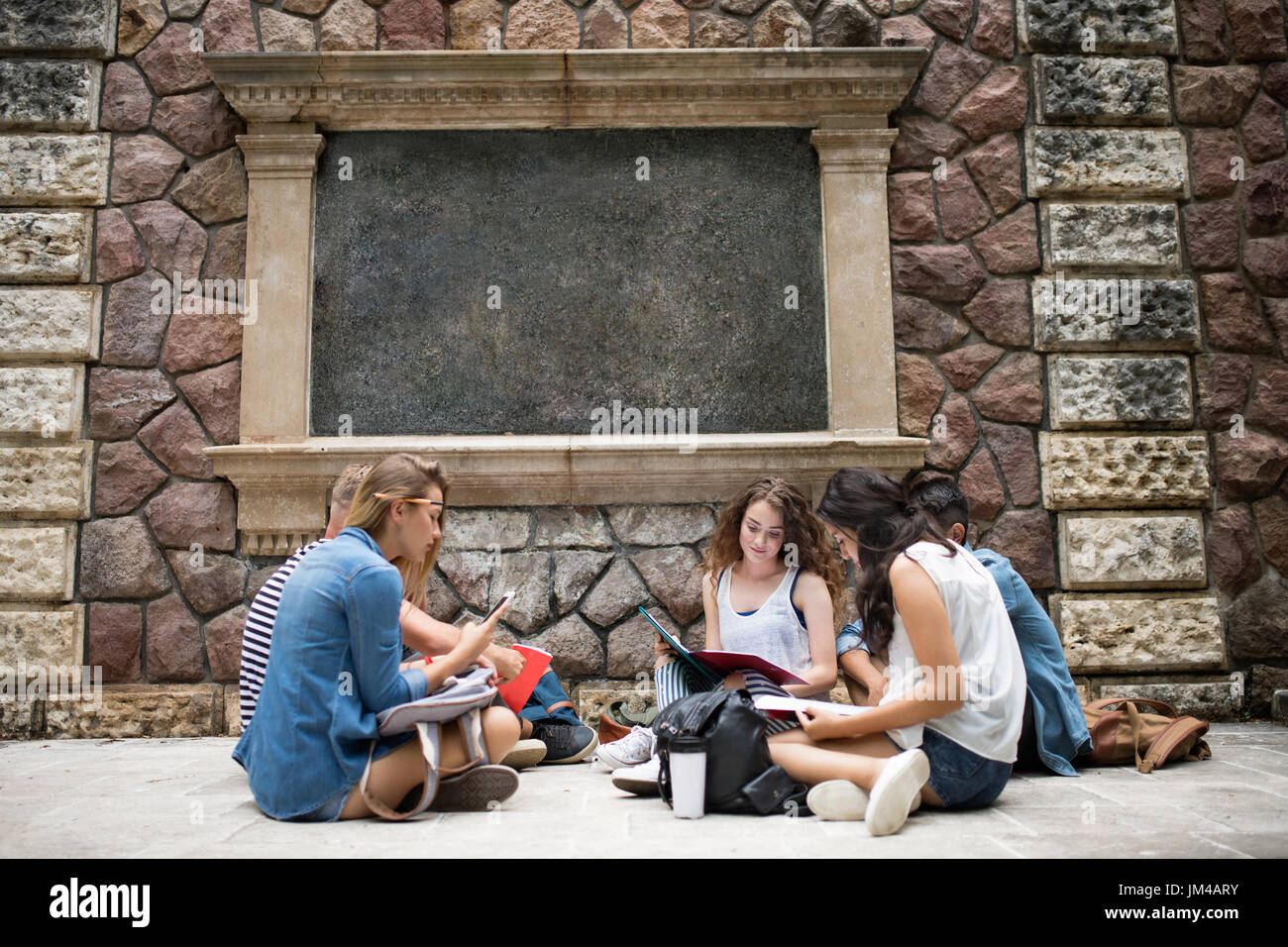 Group of attractive teenage students sitting on the ground in front of ...