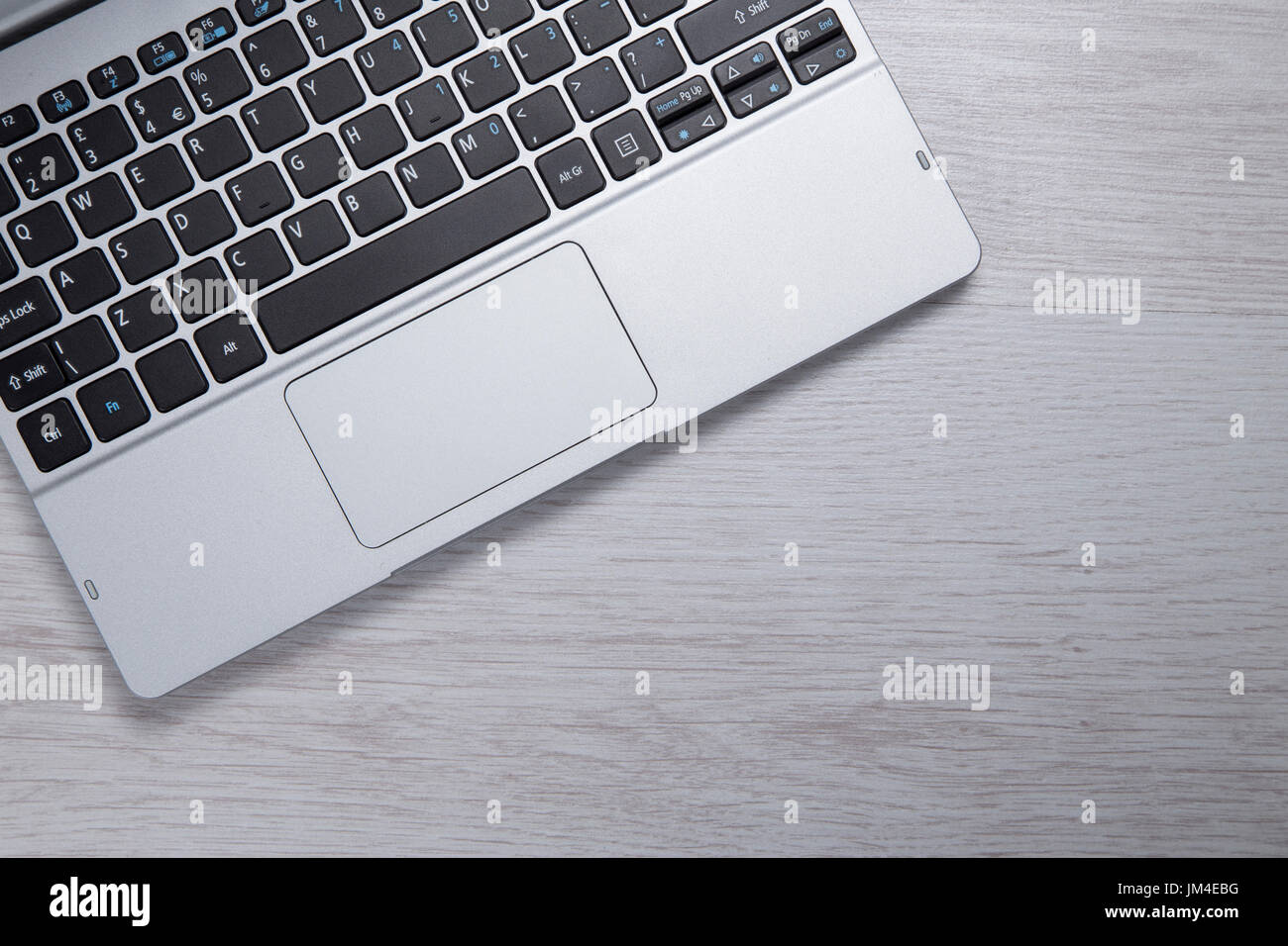 Grey toned overhead view of an open laptop keyboard on a wood grain ...
