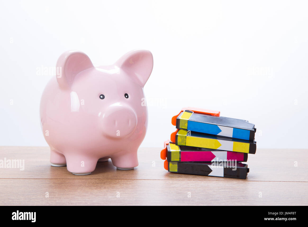 Cute pink piggy bank with a stack of generic ink cartridges for a ...