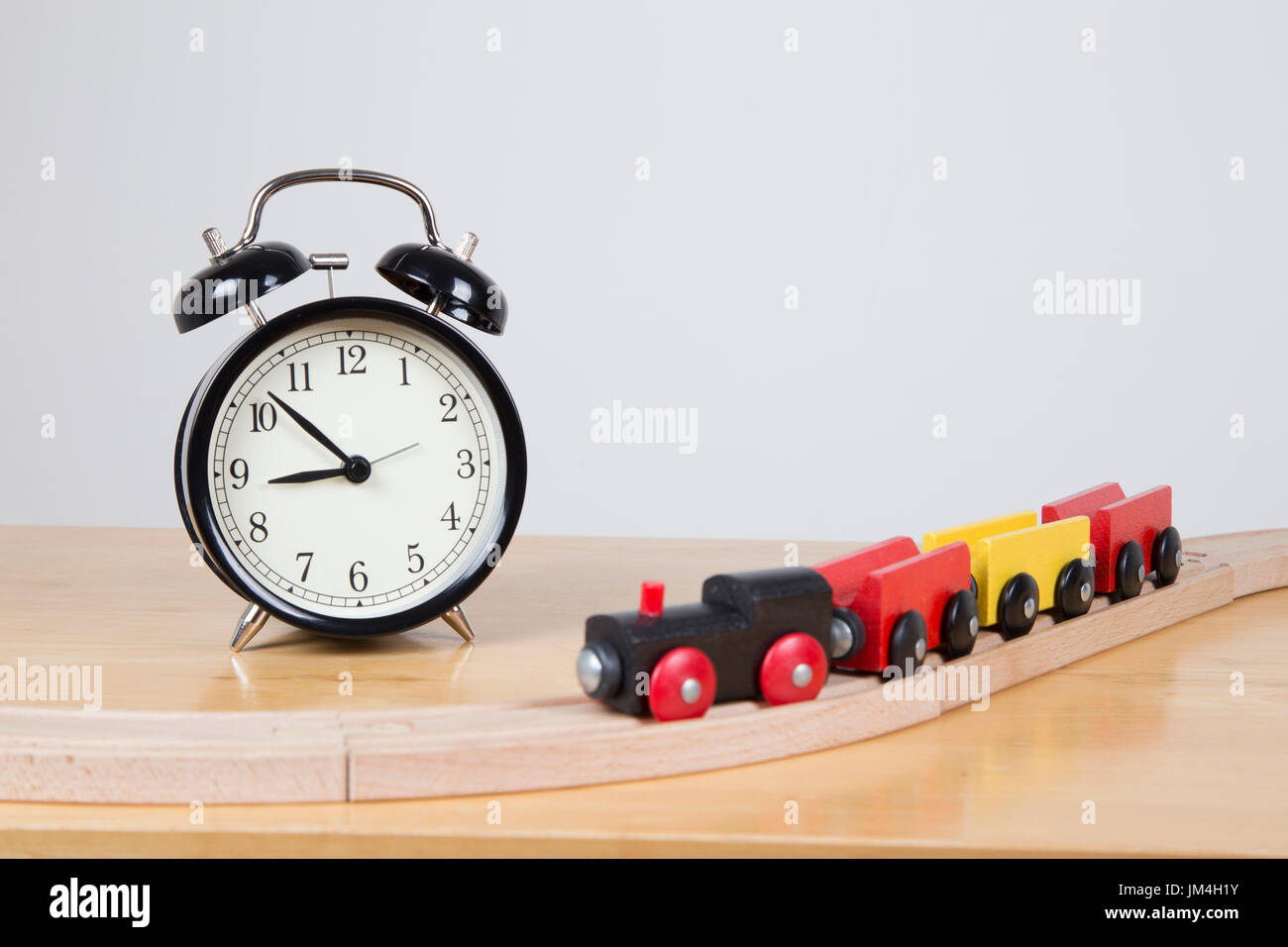 Wooden toy train passes a black alarm clock Stock Photo - Alamy