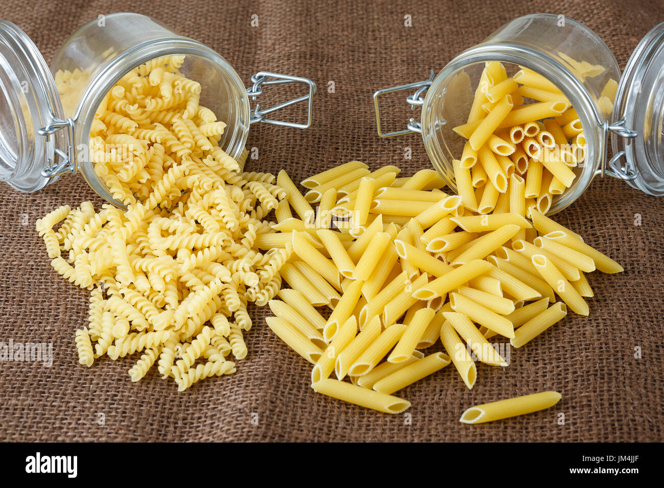 Italian pasta - penne and fusilli in glass jar on brown background ...