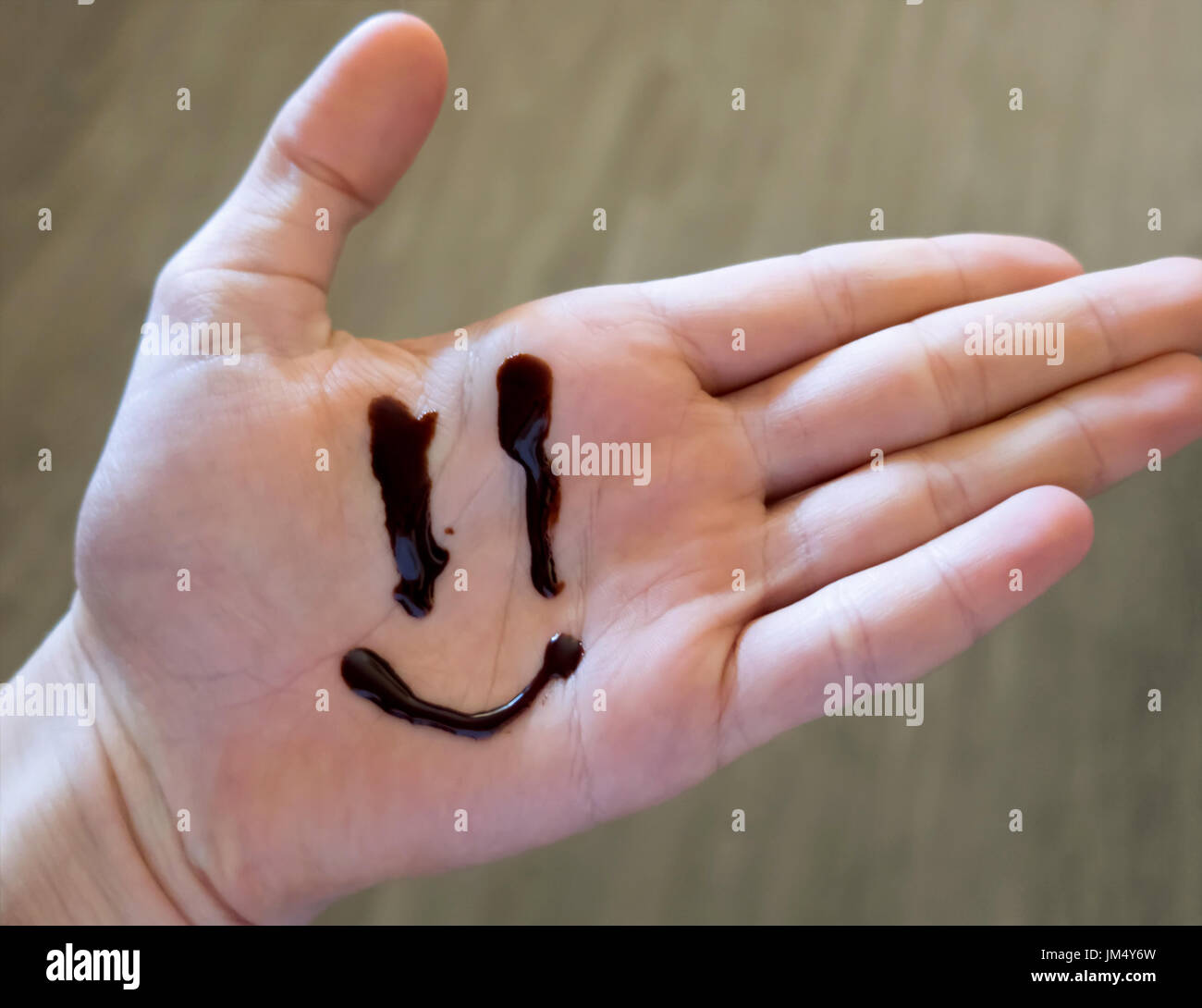 A smiley face drawn with syrup on a hand Stock Photo - Alamy