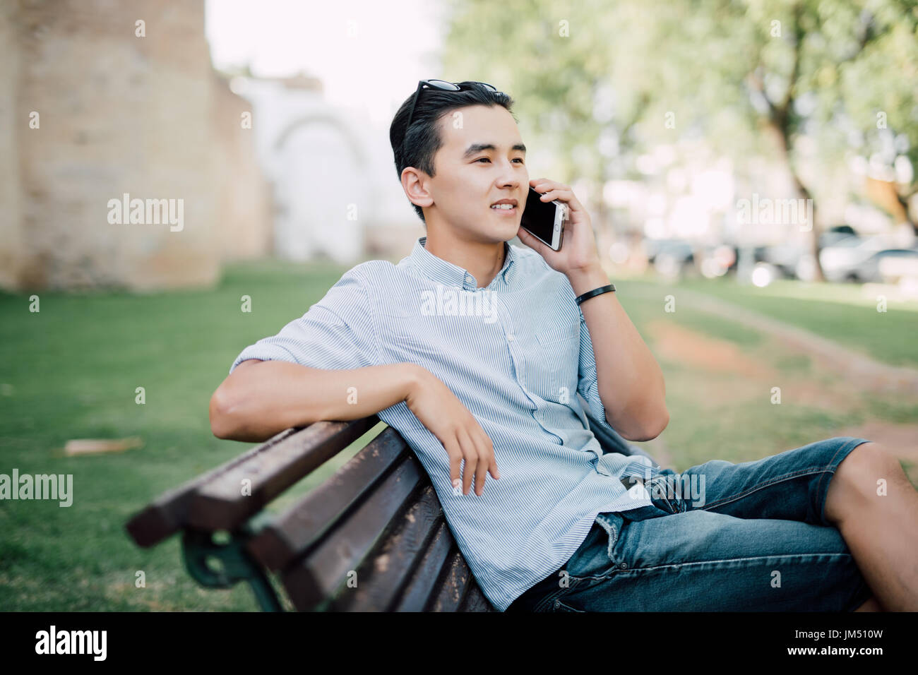 Portrait of a happy man sitting on the bench talking on the phone ...