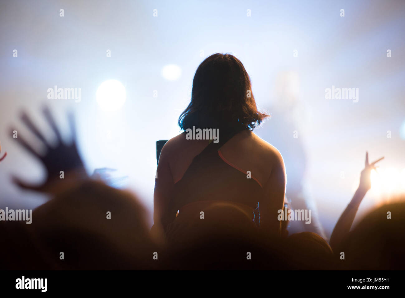 Rear view of crowd with arms outstretched at concert. Bright stage ...