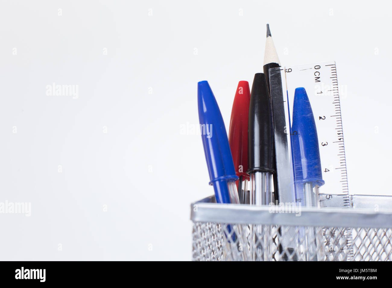 Metal mesh desk tidy with several ballpoint pens, a pencil and ruler ...