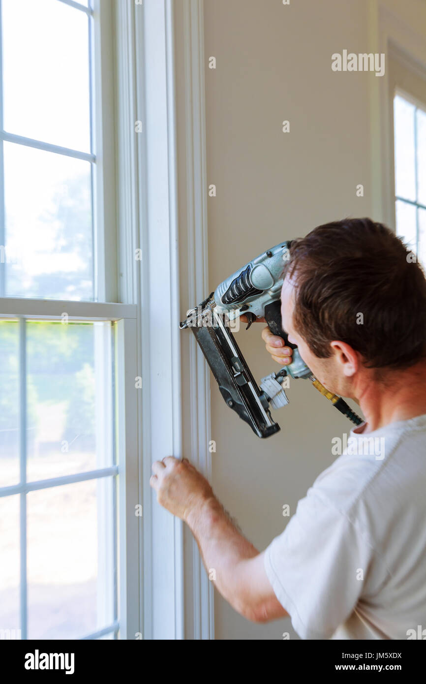 Carpenter using nail gun to moldings on windows, framing trim, with the ...