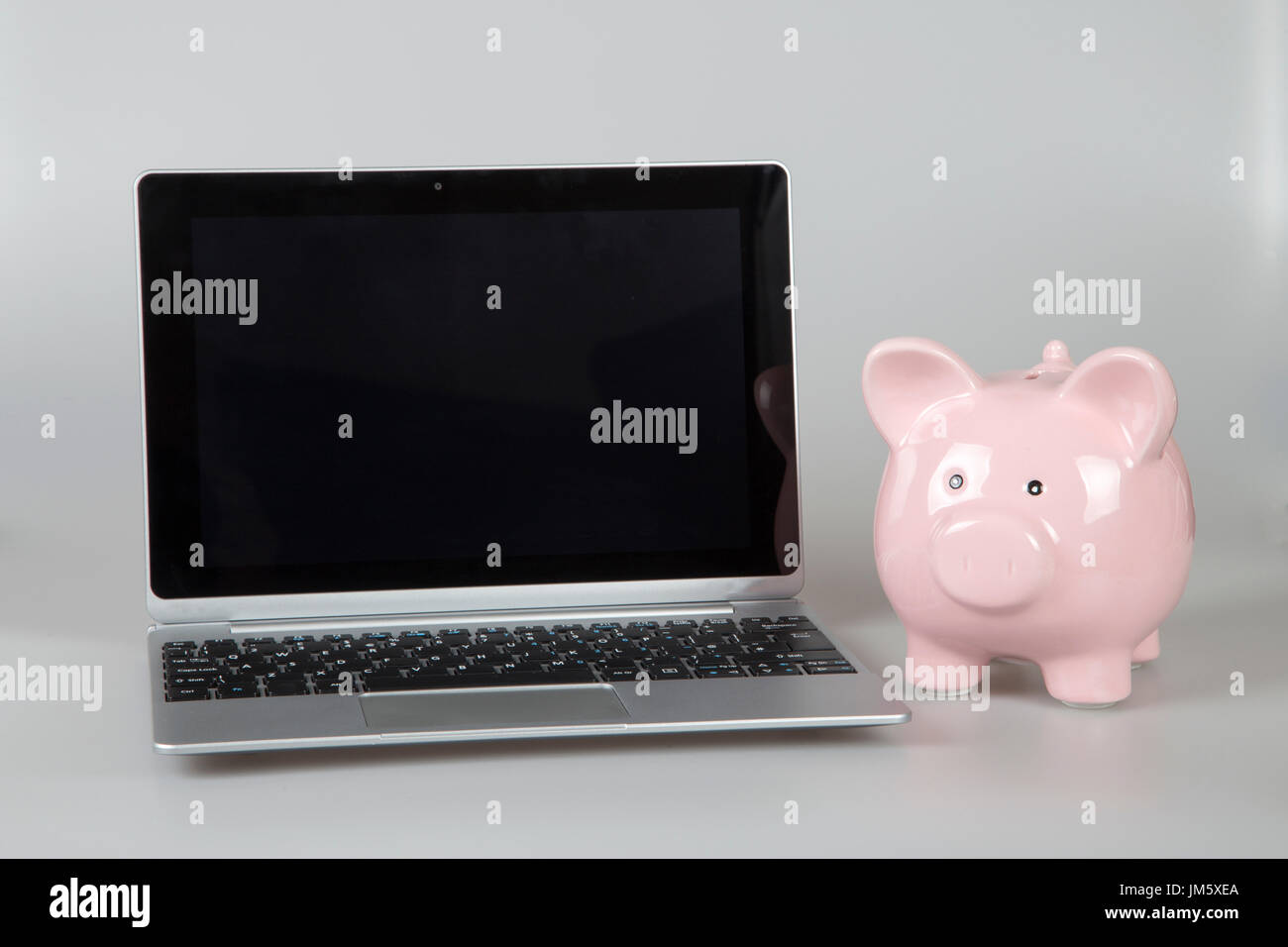 Pink piggy bank standing next to open laptop Stock Photo - Alamy