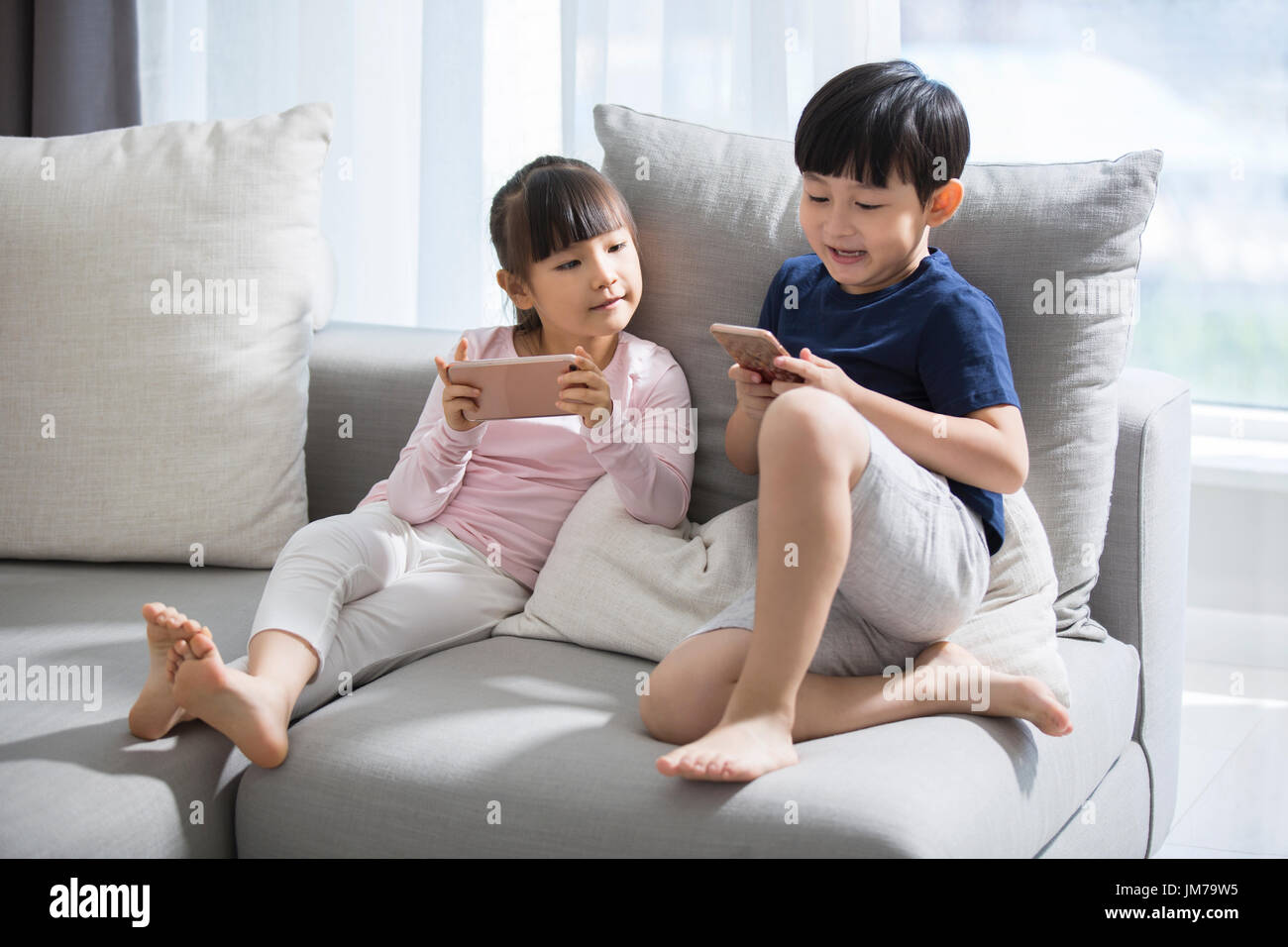 Happy Chinese boy and girl playing smart phones in sofa Stock Photo - Alamy