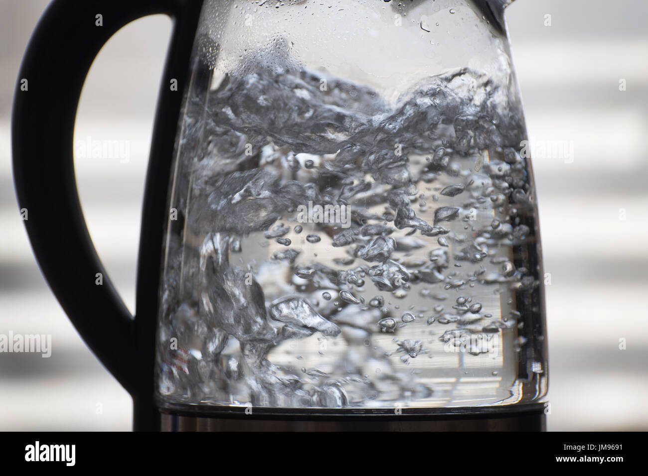 Horizontal closeup of water boiling in a glass vessel, with a light ...