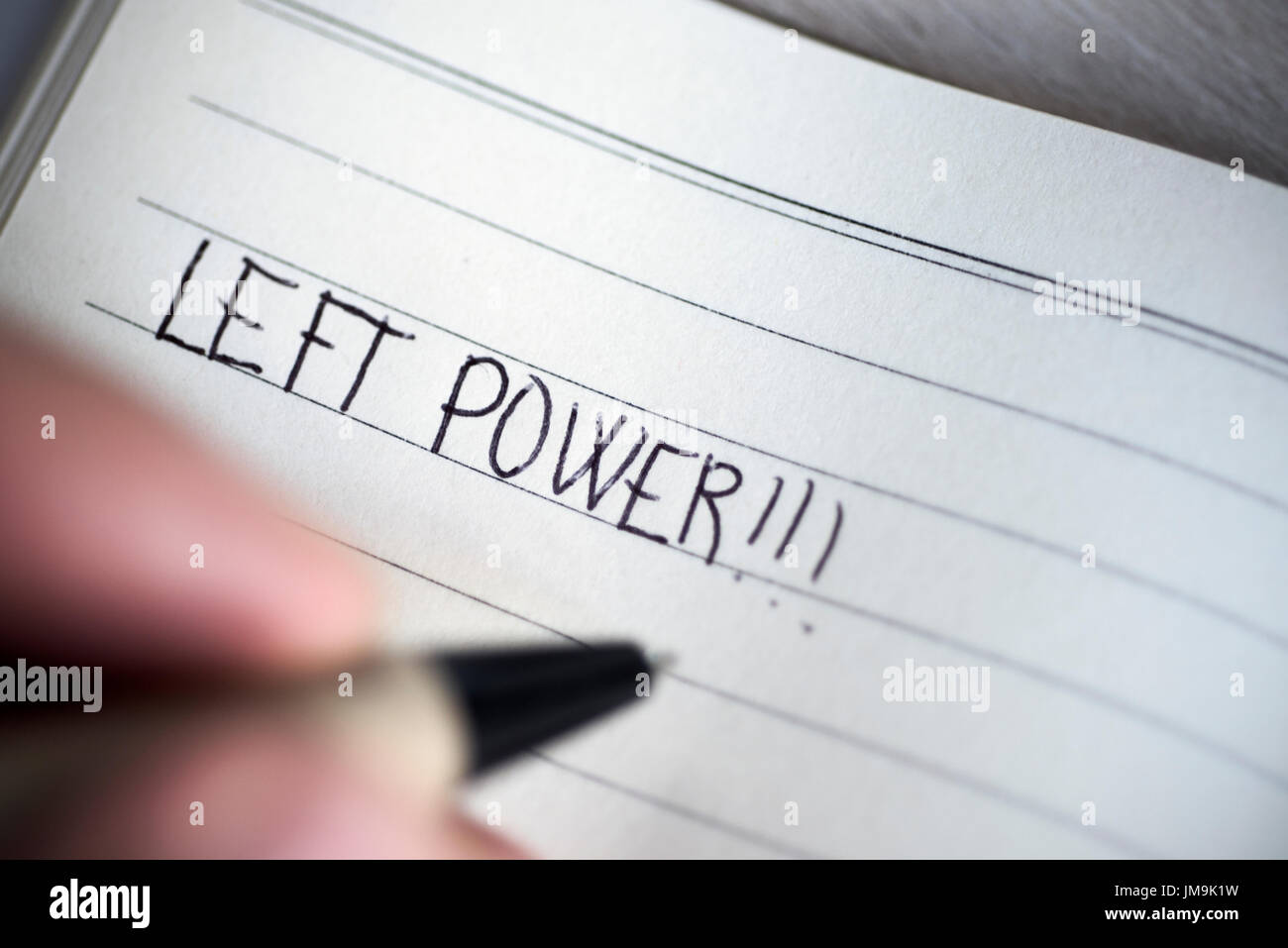 closeup of a young left-handed man handwriting the text left power in a ...