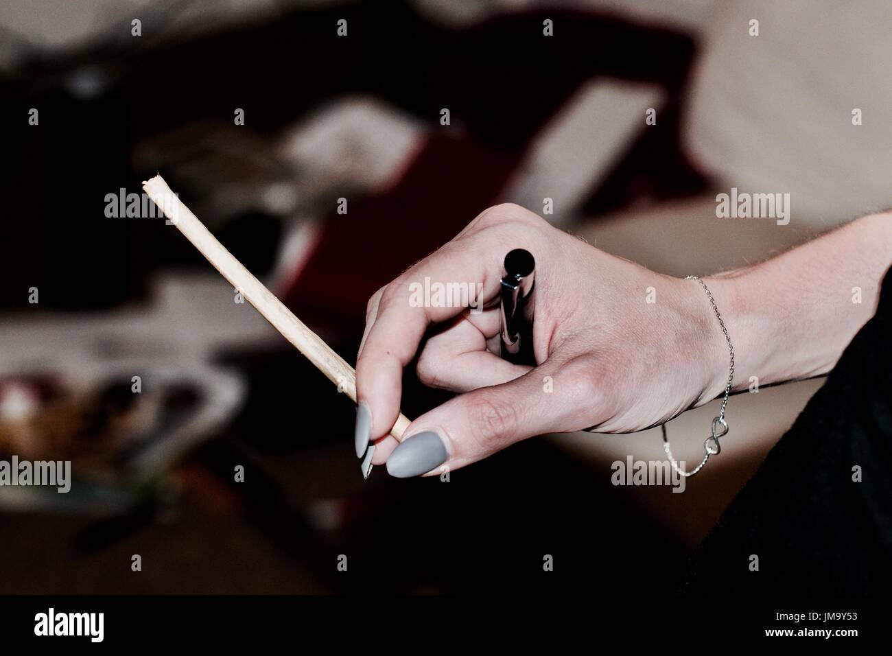 Woman hand with infinity bracelet black pencil and long marijuana joint ...