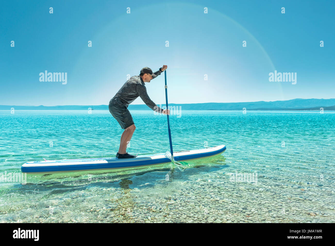 Side view of man on a Stand up Paddle, stroking the stinging paddle ...