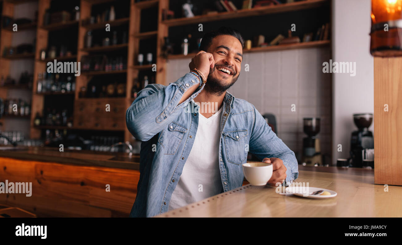 Indoor shot of smiling young man sitting at coffee shop and talking on ...