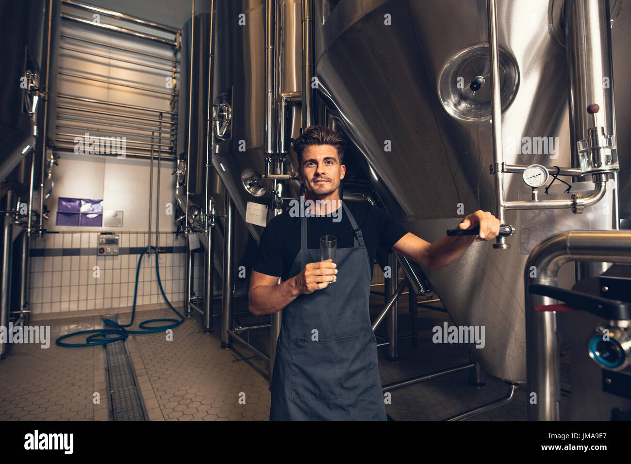 Portrait of male brewer standing by tank in brewery. Man examining the ...
