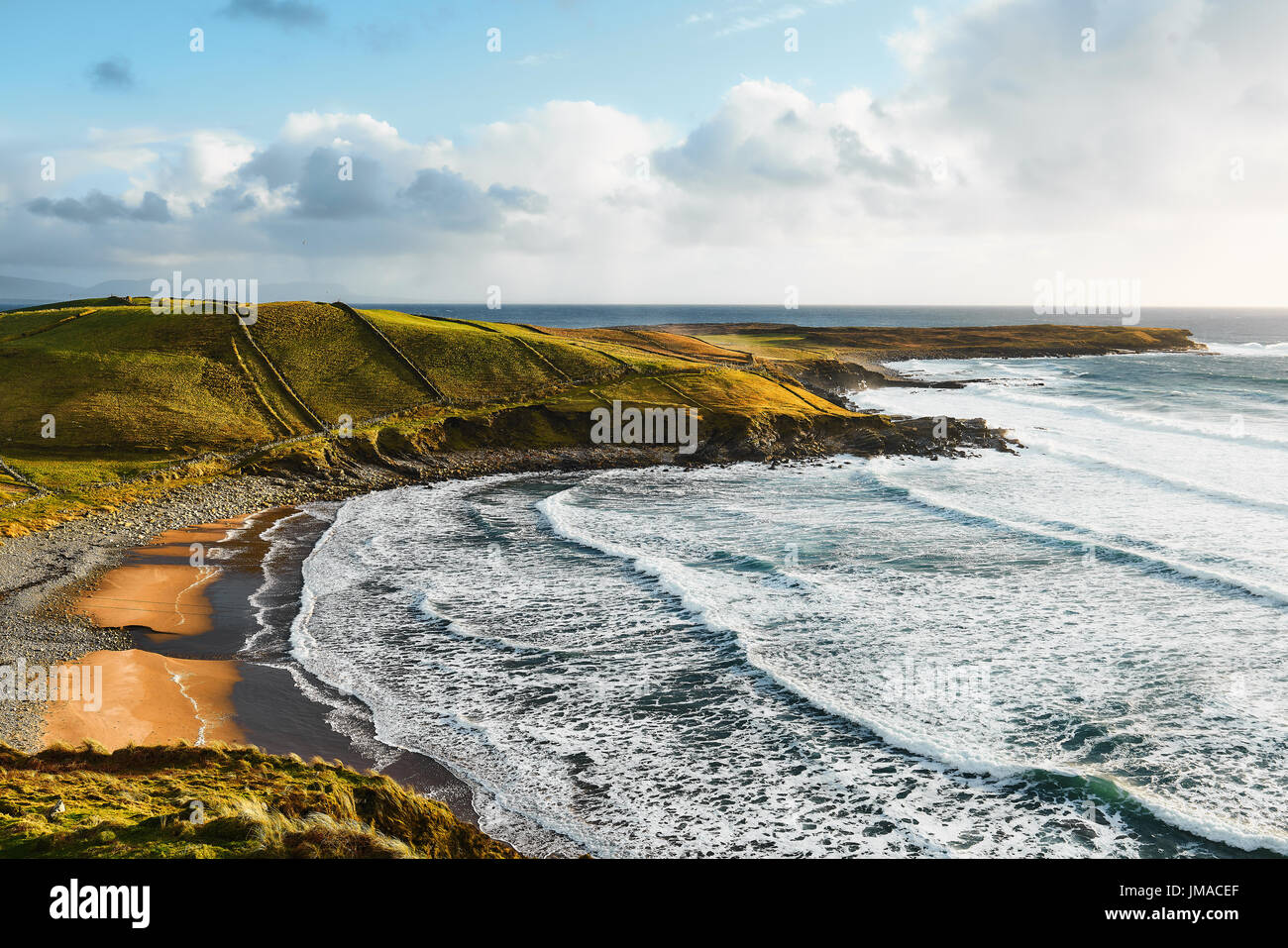 Irish beach during sunset in the summer with a blue sky and waves ...