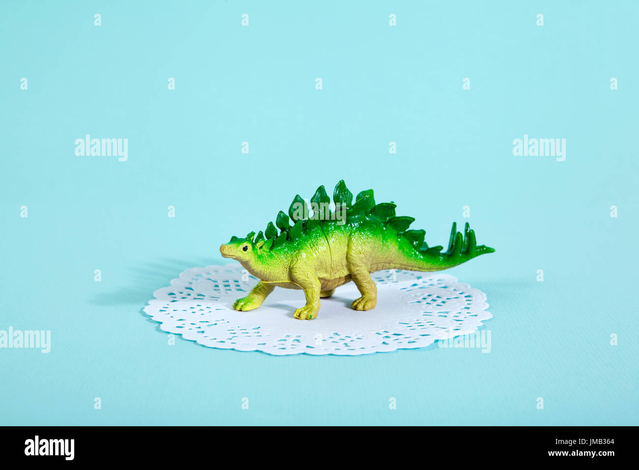 A dinosaur stegosaurus on a white lace paper doily with a vibrant ...