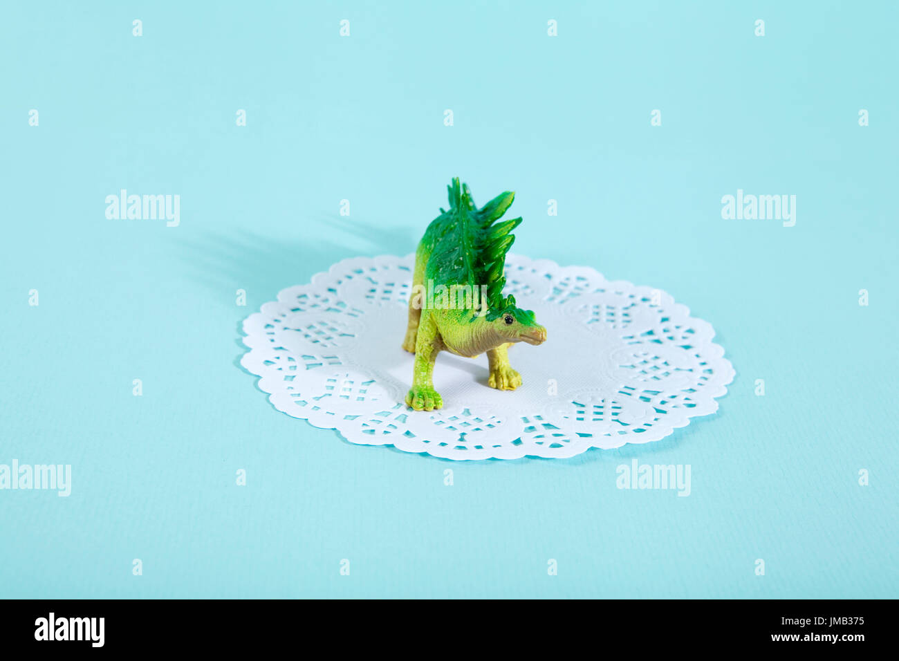 A dinosaur stegosaurus on a white lace paper doily with a vibrant ...