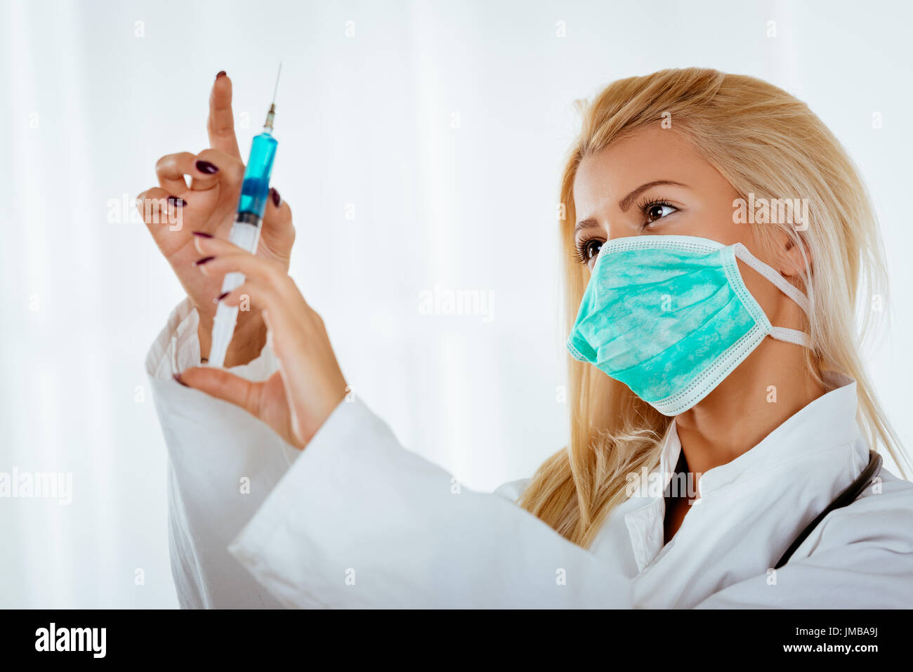 Beautiful young woman in a white coat preparing an injection of ...