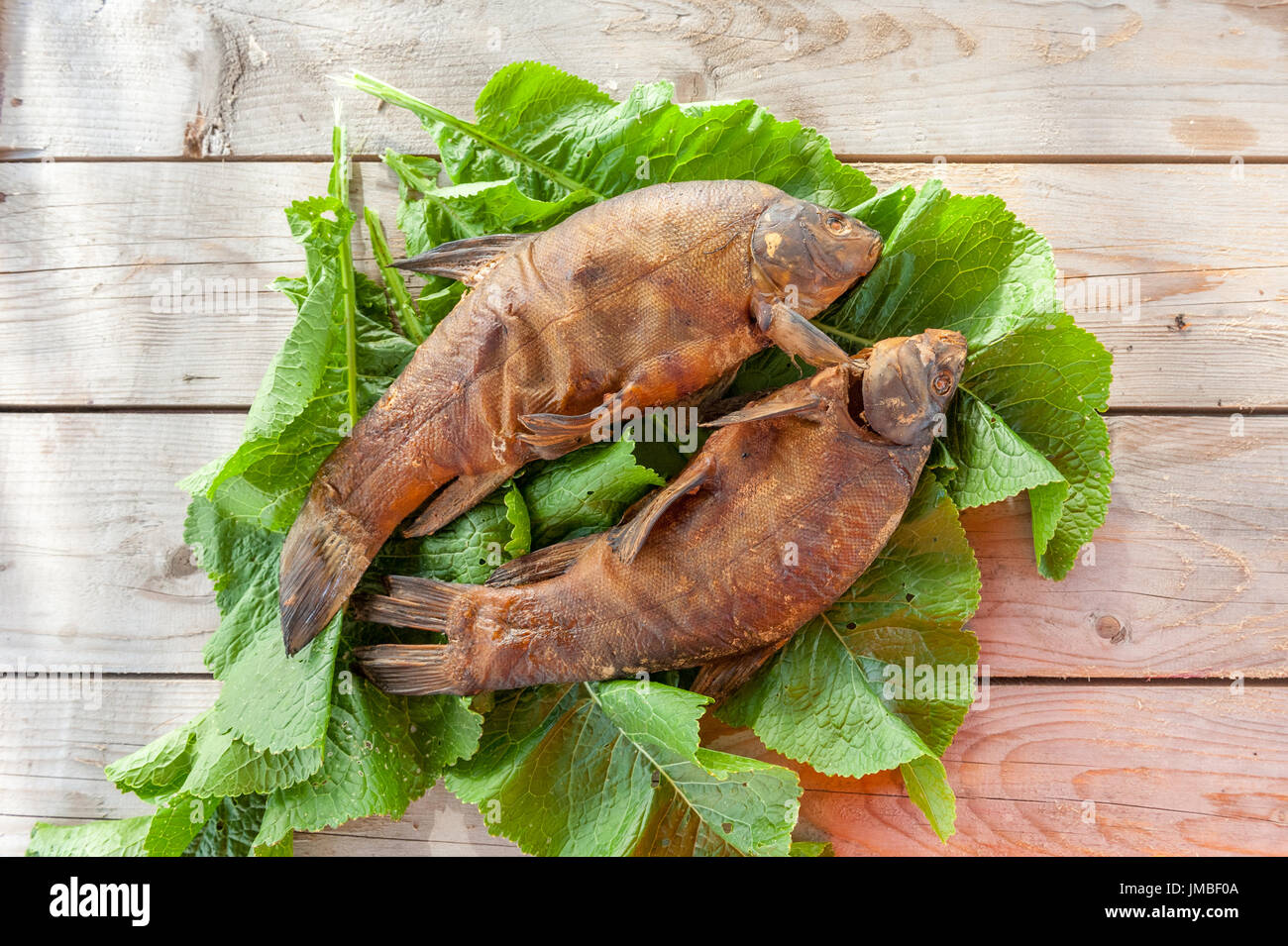The smoked baked fish is laid out on green leaves lying on coarse ...