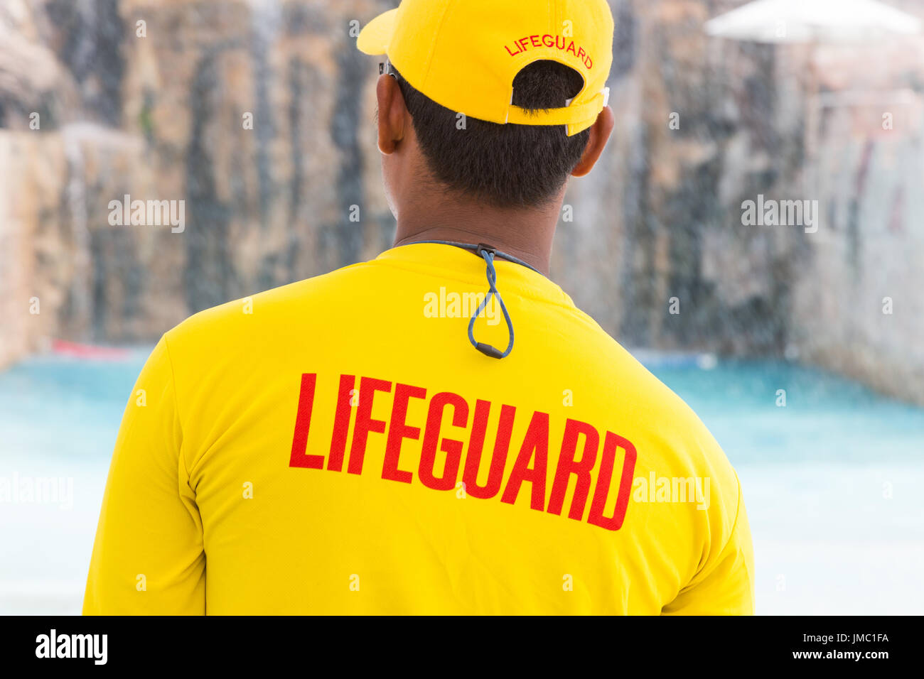 back side of lifeguard man wearing yellow lifeguard shirt and cap ...