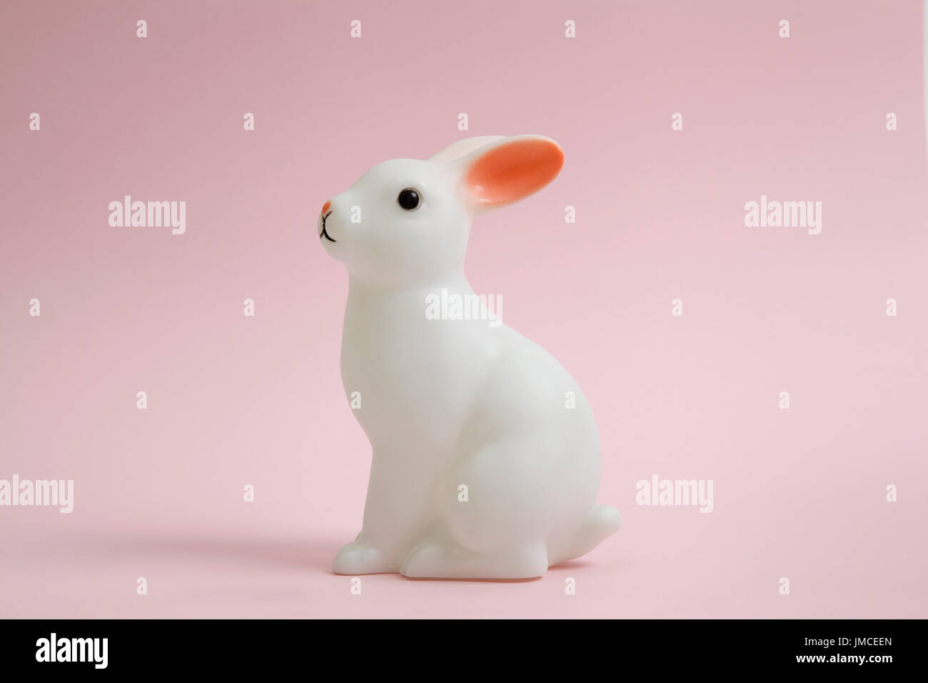 a cute white plastic bunny on a pink background. Minimal color still ...