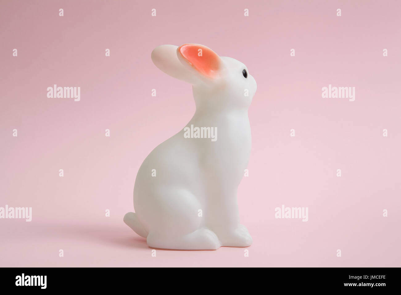 a cute white plastic bunny on a pink background. Minimal color still ...