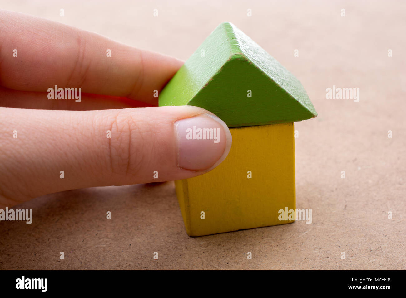 Hand holding a house formed out of building blocks s on a brown ...