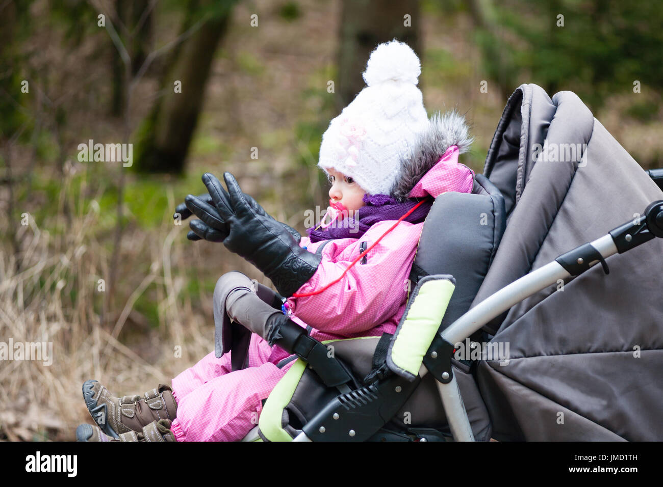 girl child is sitting in the buggy in the park at spring and smiling ...